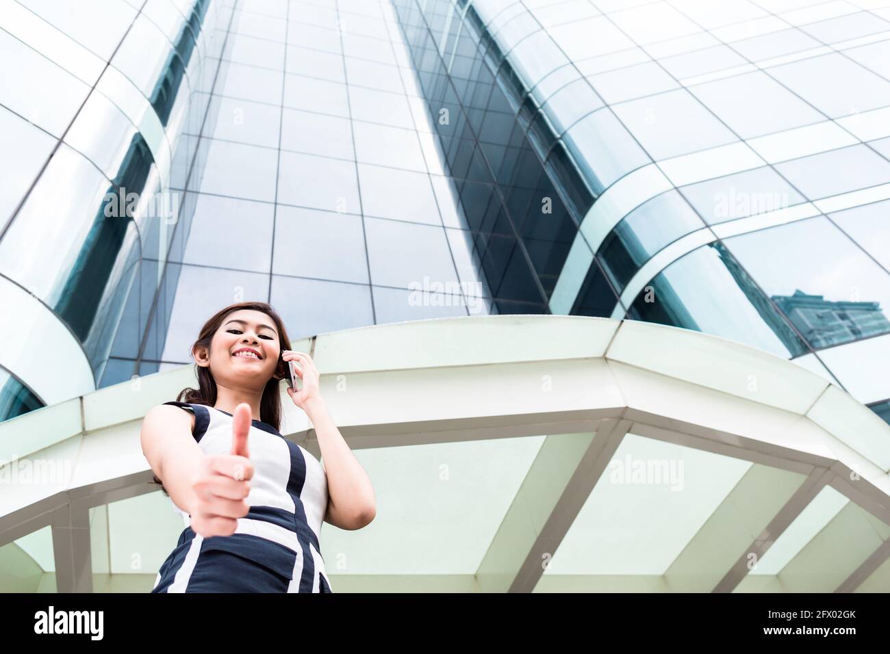 Asian businesswoman telephoning wit smartphone in front of tower ...