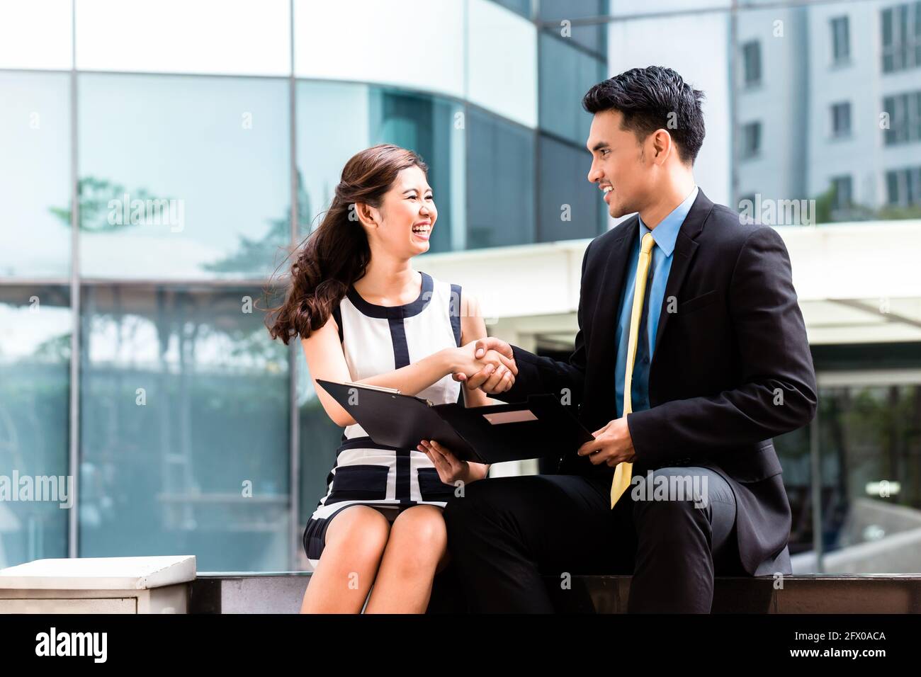 Asian business men and woman outside in front of tower building shaking ...