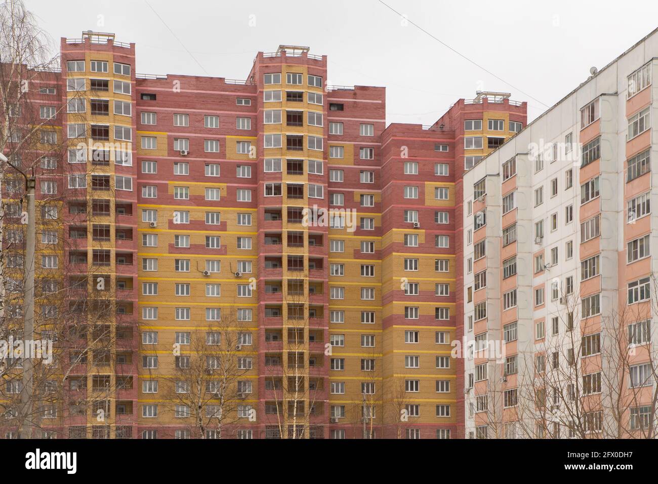 High-rise new building with red balconies next to an old gray house ...