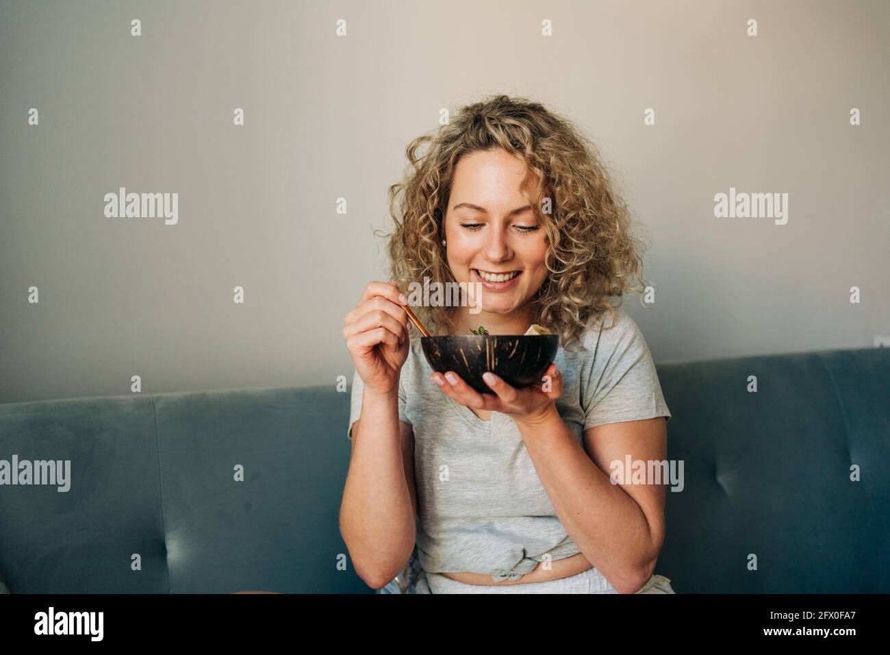 Cheerful female in domestic wear enjoying yummy food in bowl while ...