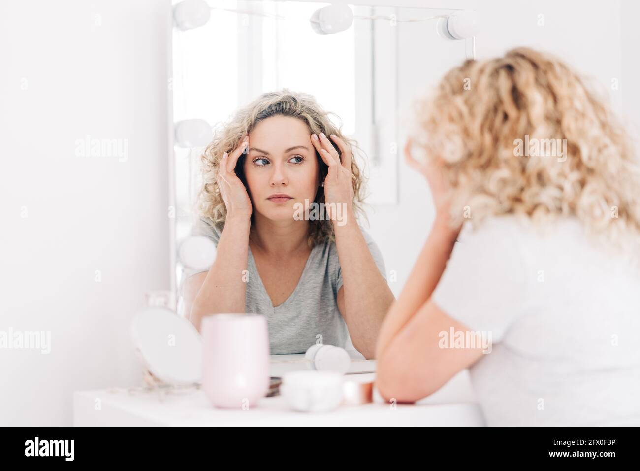 Unemotional attractive female in casual shirt touching face and looking ...