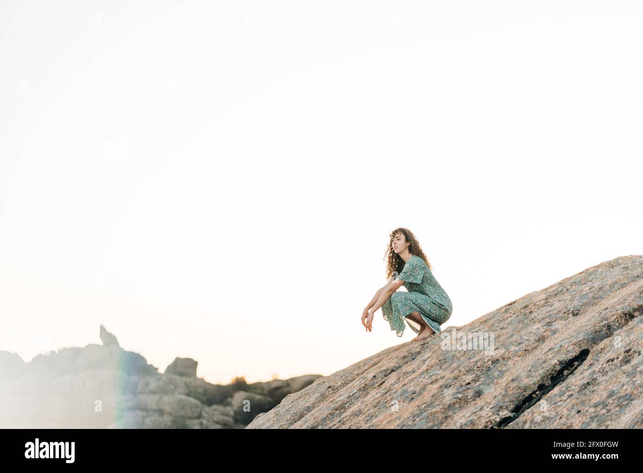 Full body attractive female in maxi sundress crouched barefoot on rough ...