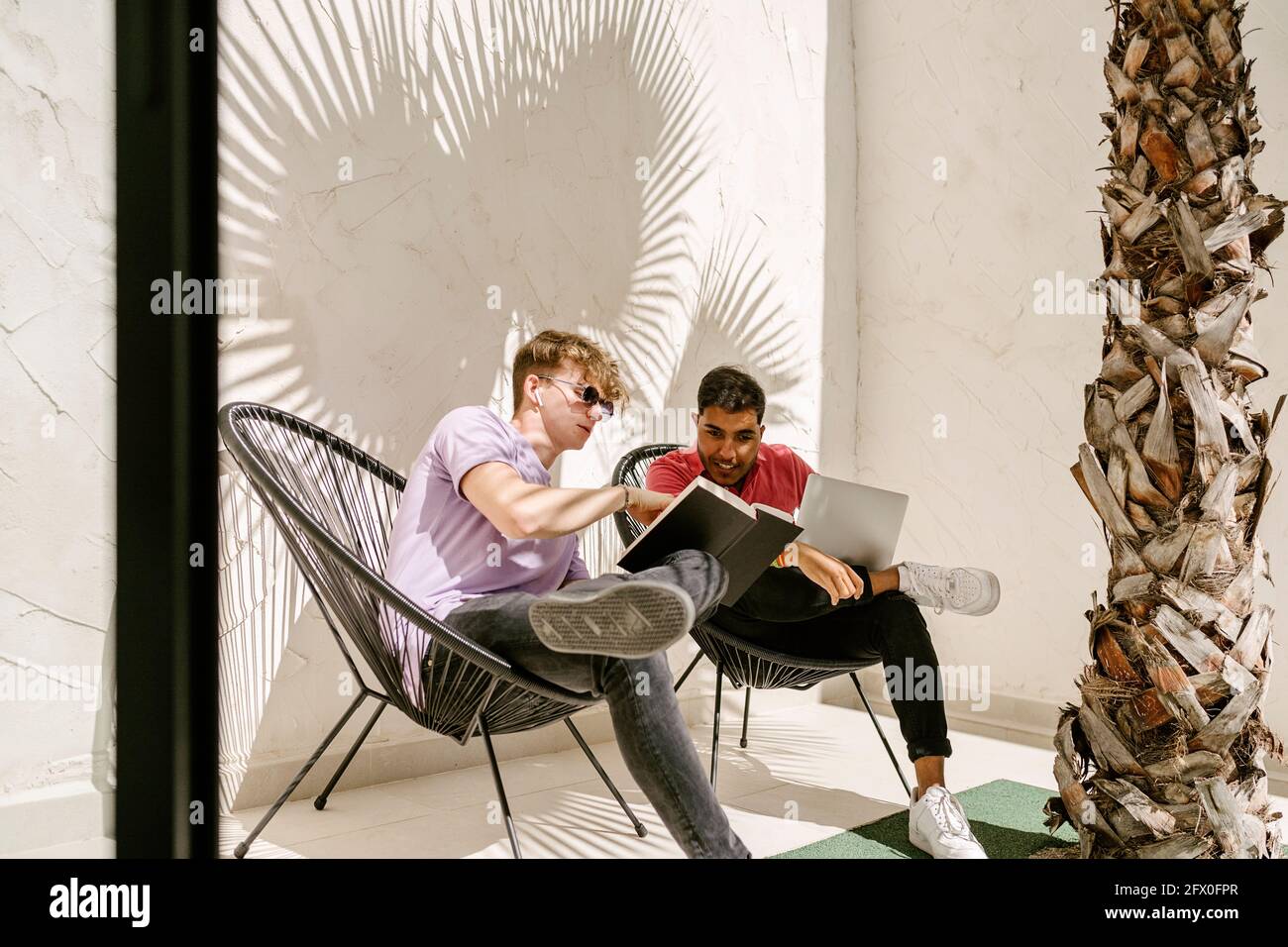 Stylish young multiracial male friends using laptop and reading book ...