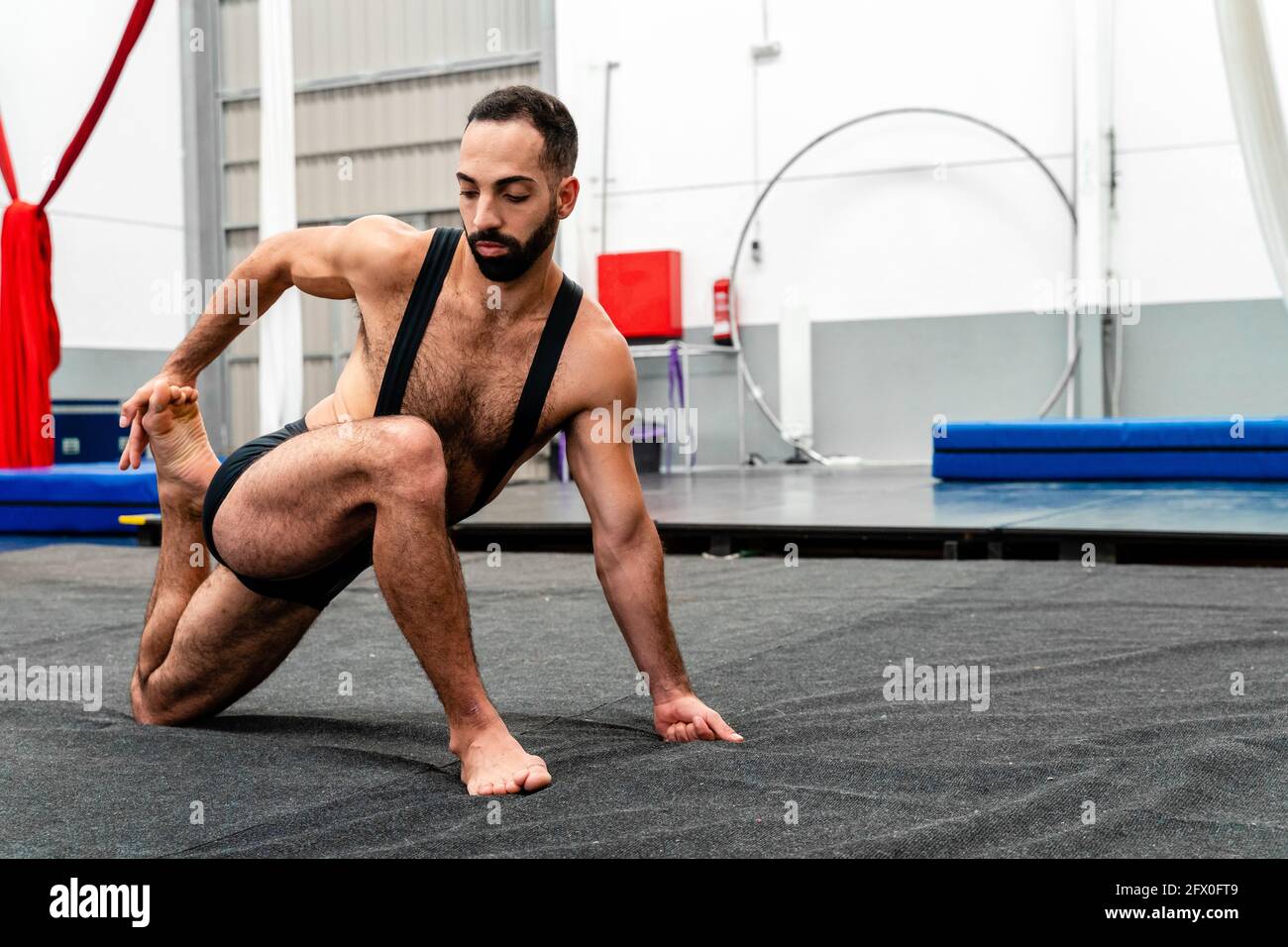 Full body muscular focused ethnic male in sports shorts performing Twisted Monkey Pose while ...