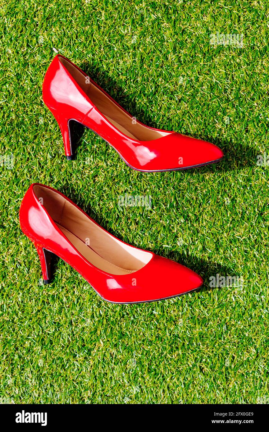 Top view of new elegant patent red shoes placed casting shadow on green ...