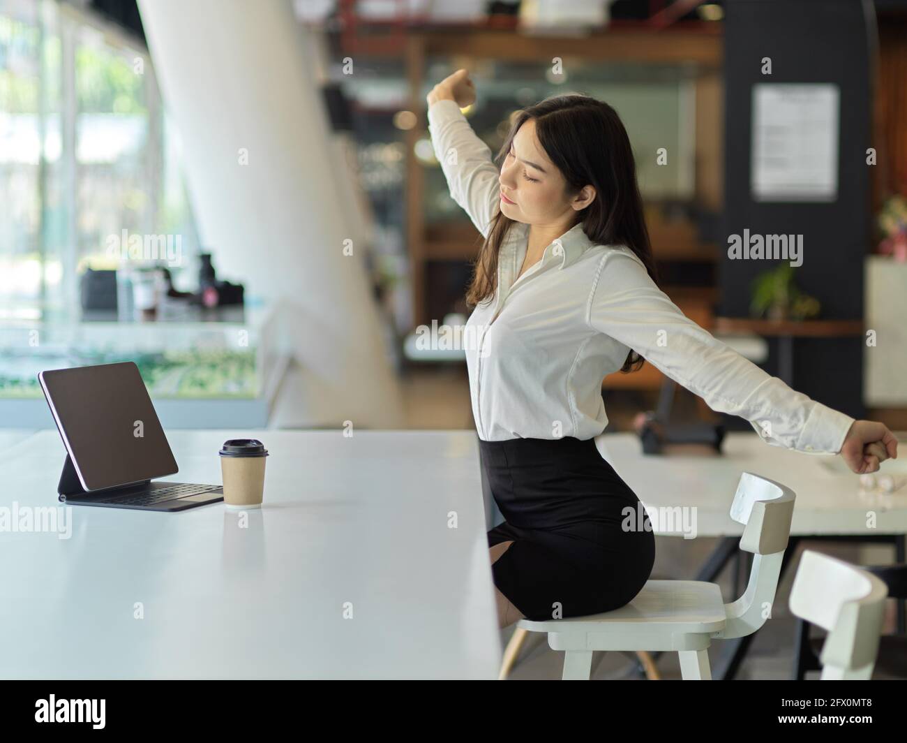 Portrait of businesswoman relaxing in office room, stretching her arms ...