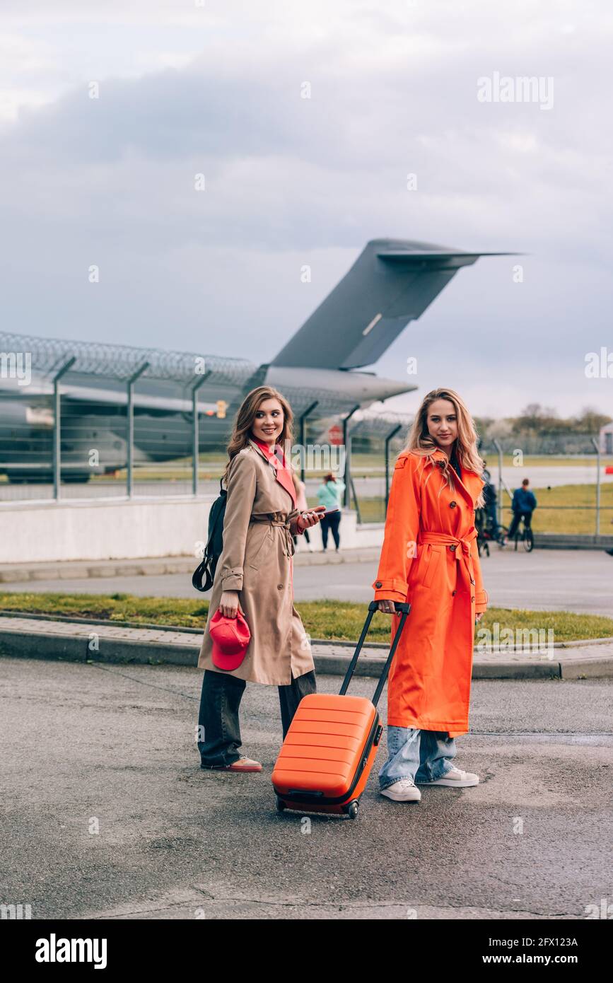Two happy girls walking near airport, with luggage. Air travel, summer ...