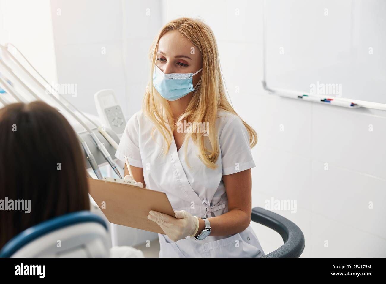 Caring female medic writing notes while staring at client Stock Photo ...
