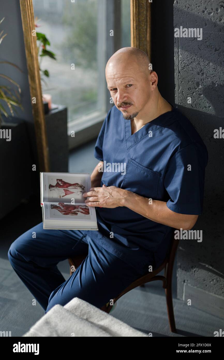 A massage therapist in a blue suit reads a book on human anatomy in his ...