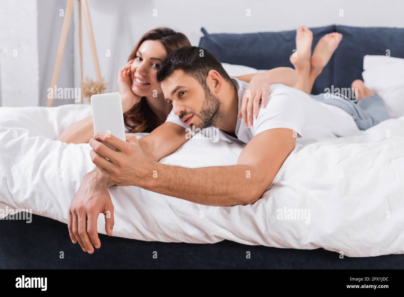 Smartphone in hand of blurred man taking selfie with girlfriend on bed ...