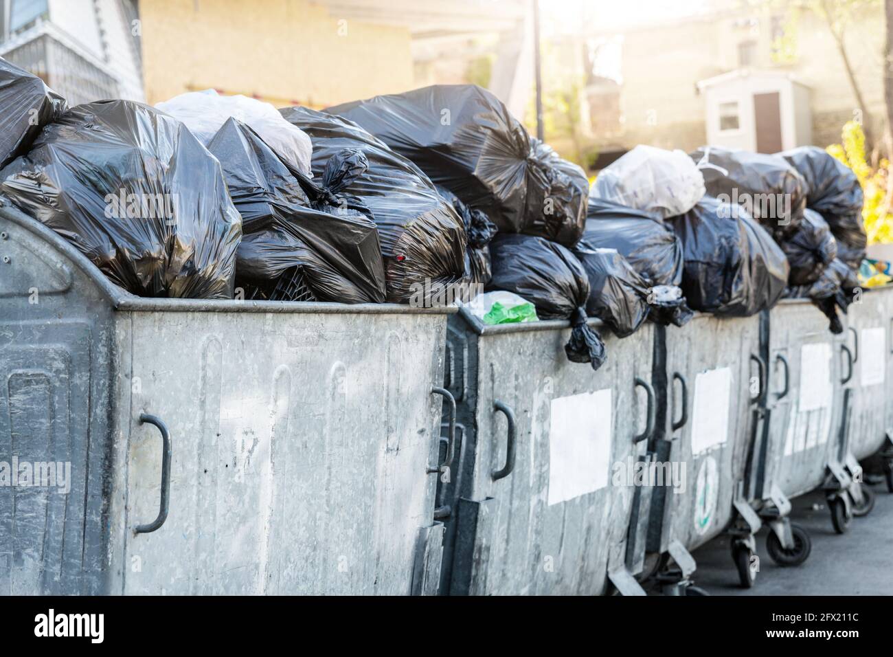 Rows of many big metal overloaded dumpster cans full of black plastic ...