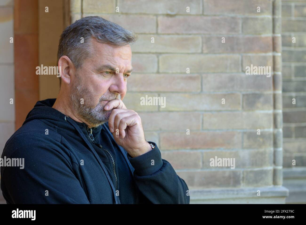 Man standing outside a brick building deep in thought with his hand to ...