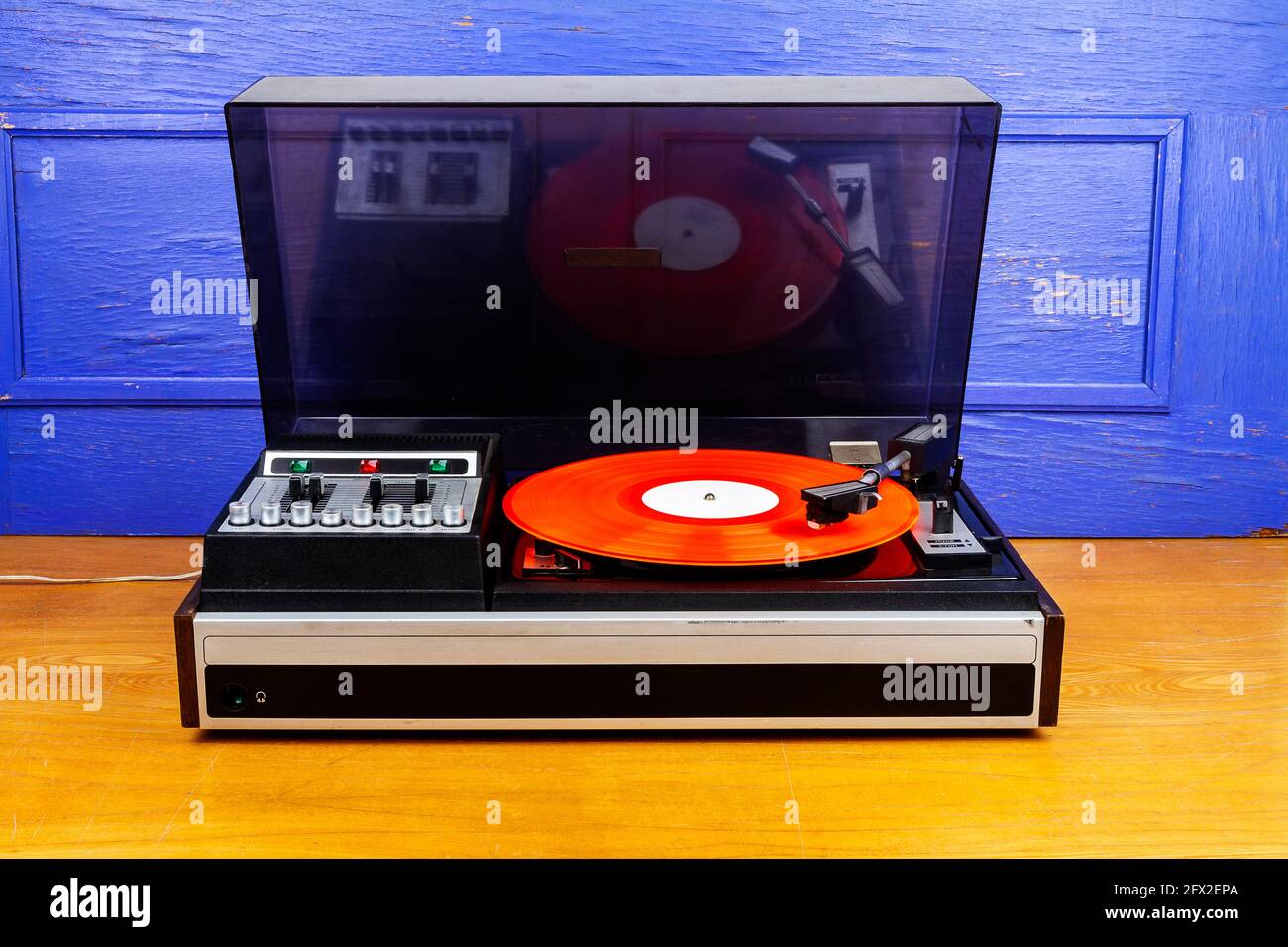 Vintage turntable vinyl record player with red vinyl on table by blue ...