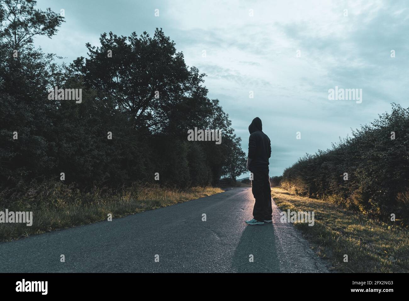 A mysterious hooded man, back to camera. looking at a long straight ...
