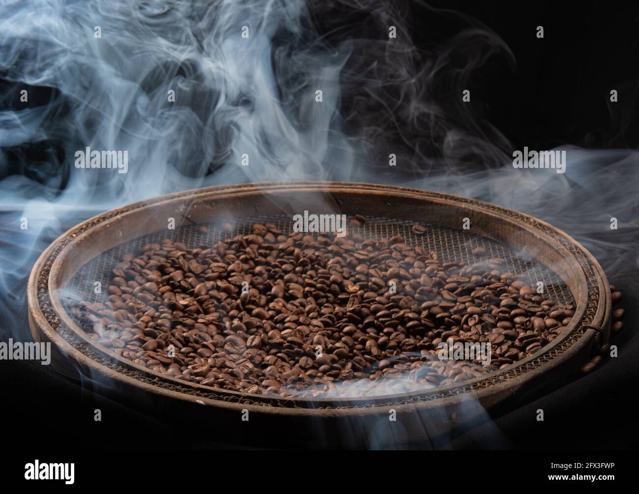 Roasted coffee on rustic sieve with smoke and with black background ...