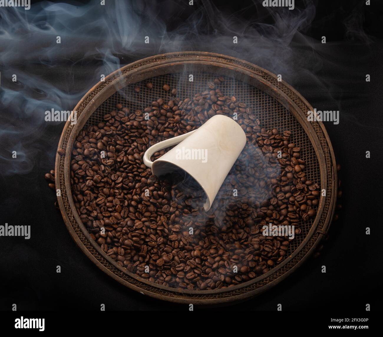 Roasted coffee on rustic sieve with smoke and a cup with black ...