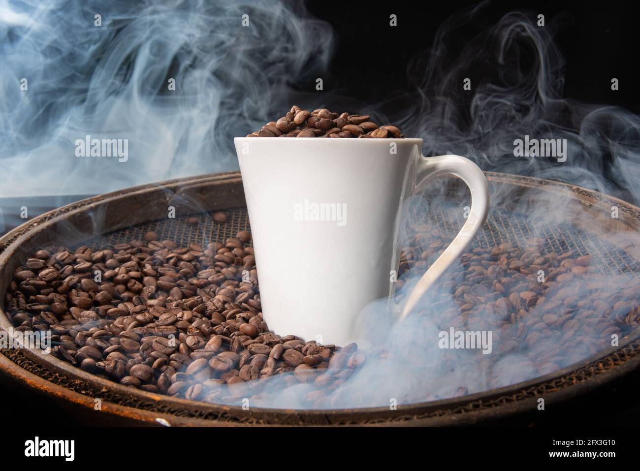 Roasted coffee on rustic sieve with smoke and a cup with black ...