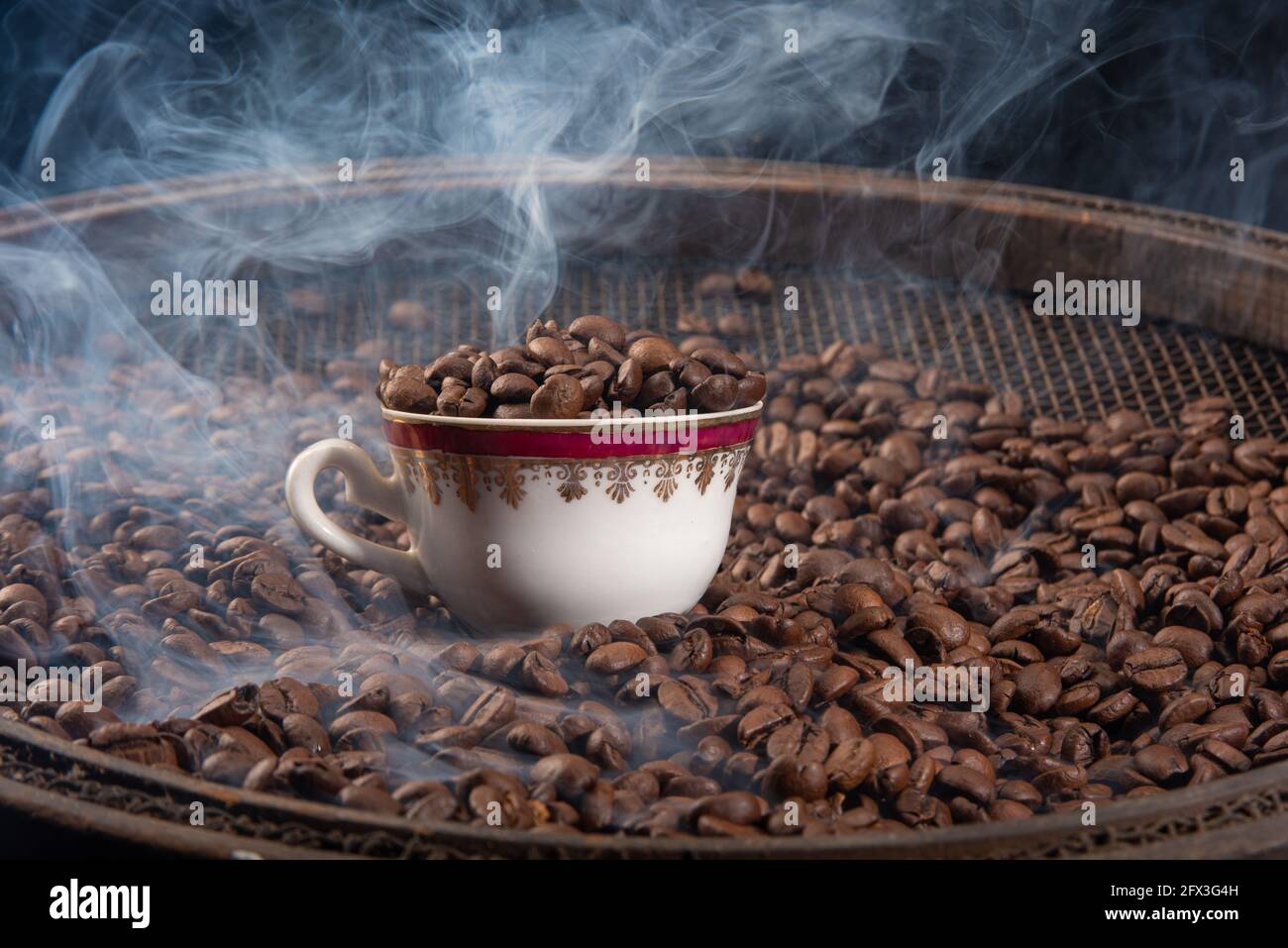 Roasted coffee on rustic sieve with smoke and a cup with black ...