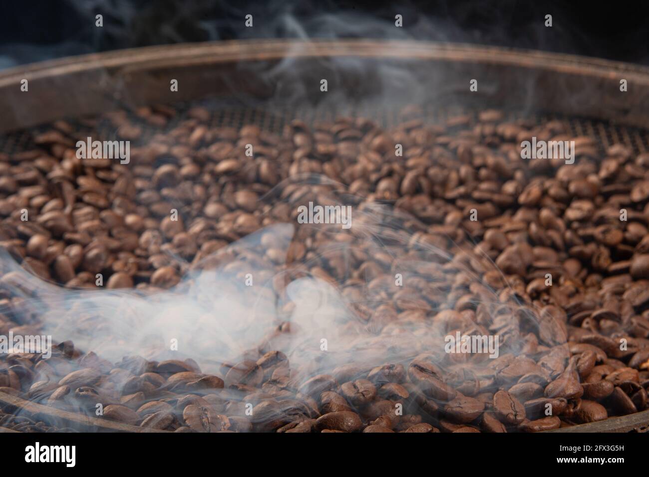 Roasted coffee on rustic sieve with smoke and with black background ...