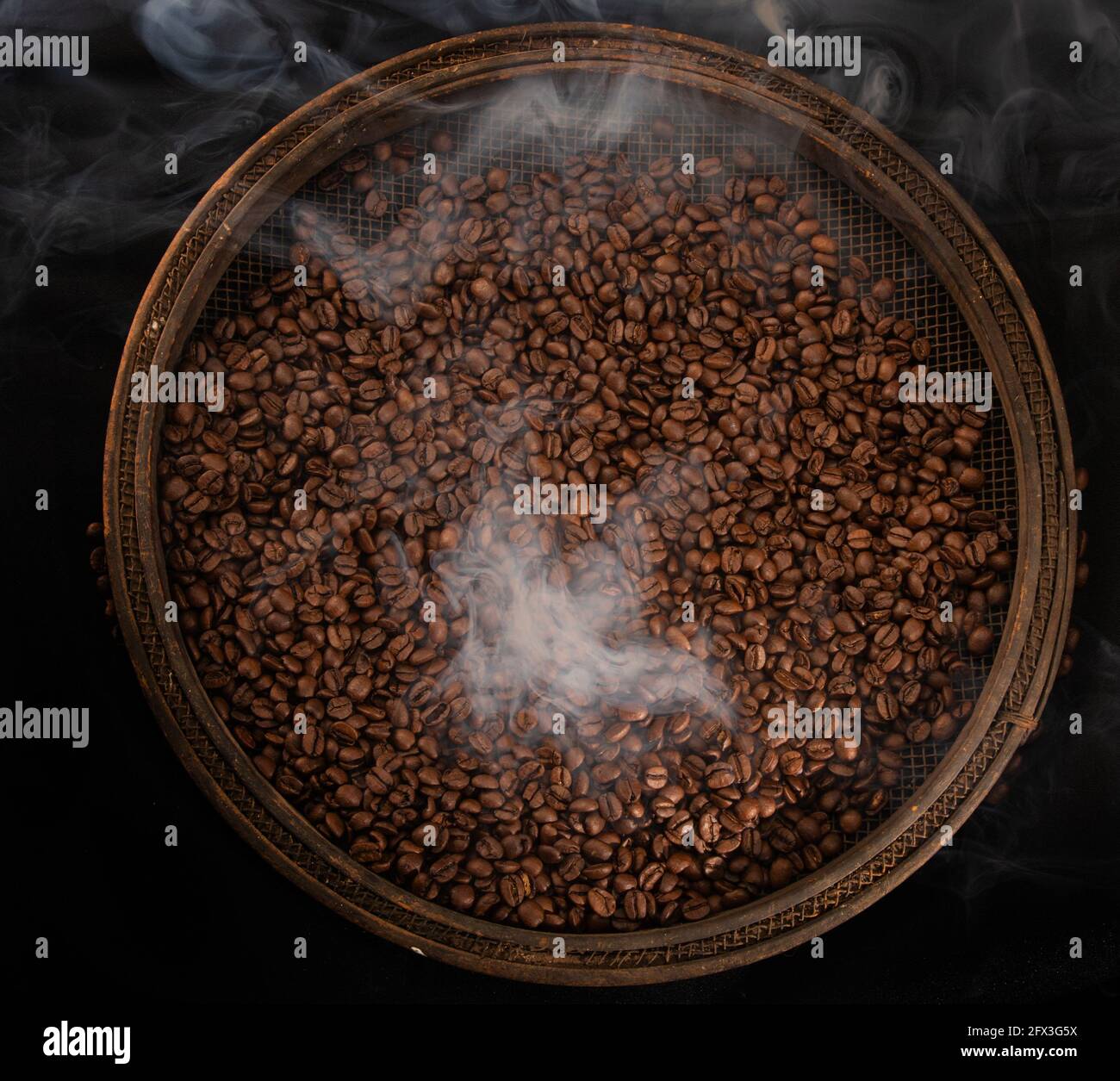 Roasted coffee on rustic sieve with smoke and with black background ...