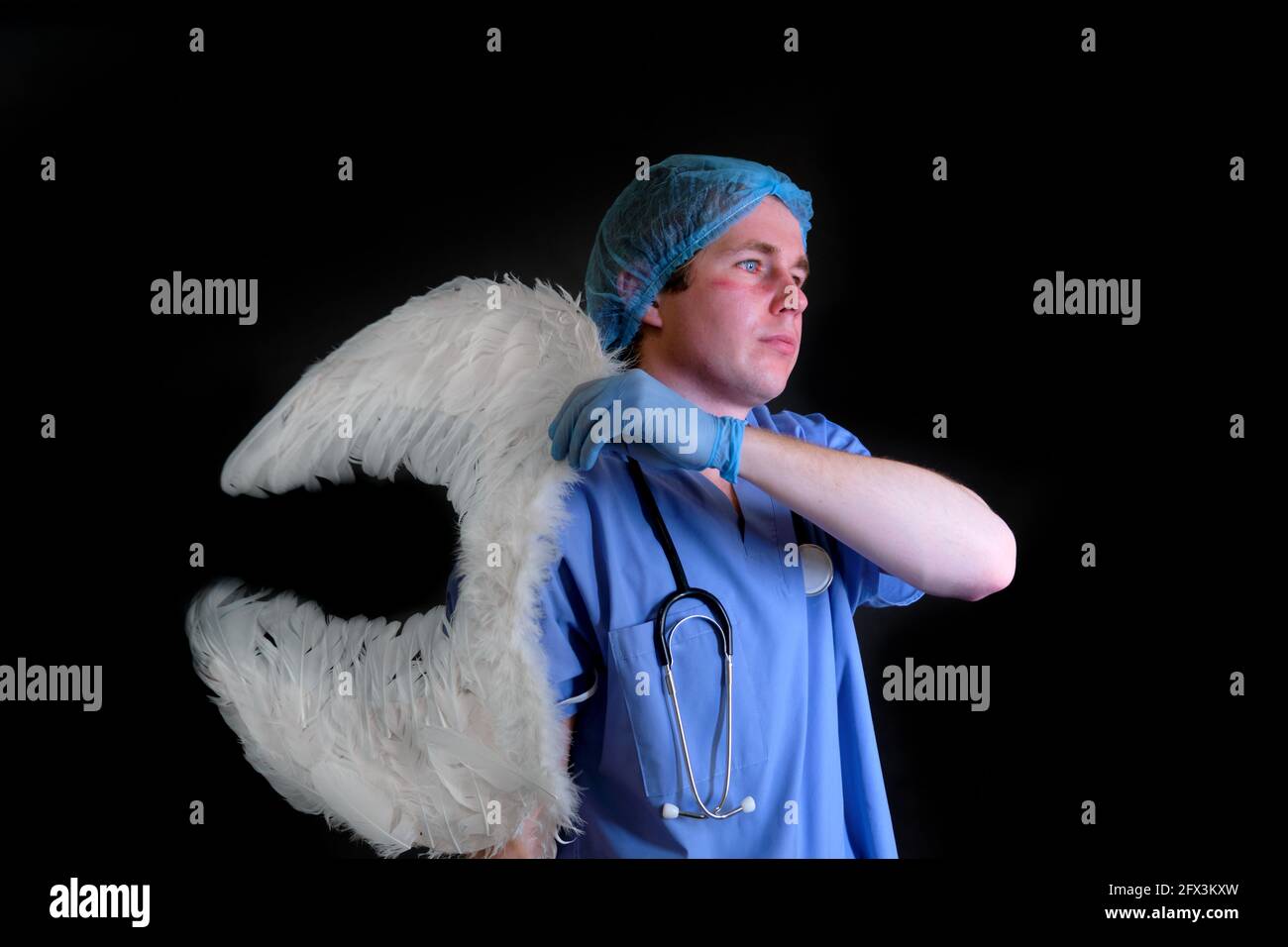 A doctor in a blue uniform puts on white angel wings on a dark ...