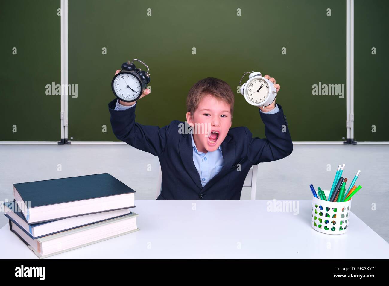 Funny junior boy with alarm clocks in the school class. Schoolboy ...