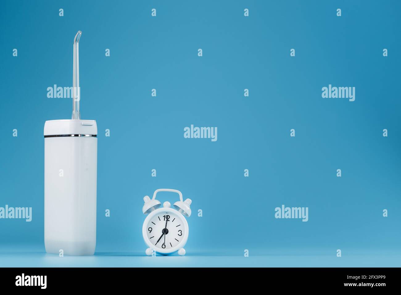 Irrigator oral cleaning with alarm clock on blue background. A mobile ...
