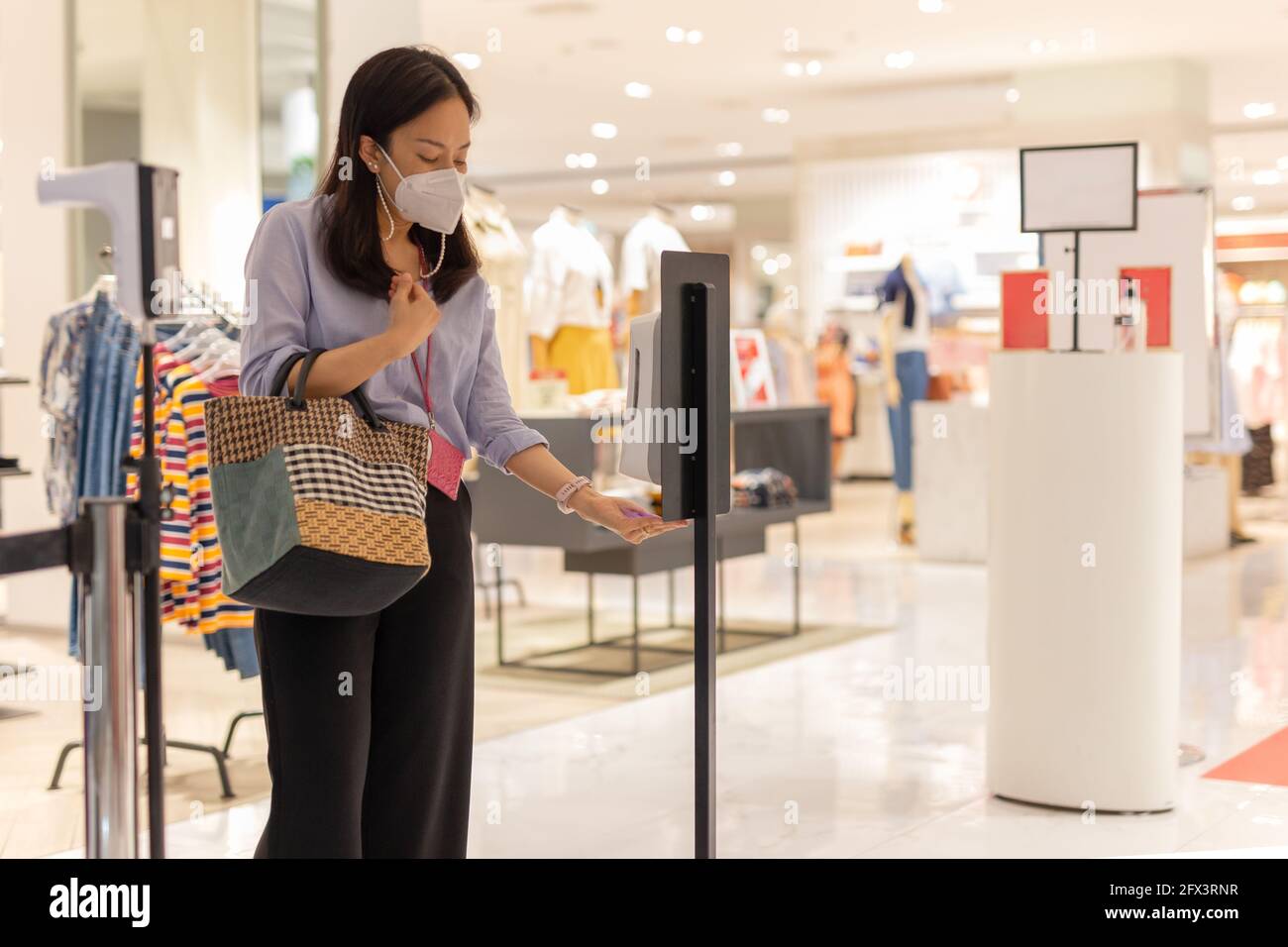 Woman in protective mask using automatic alcohol gel on her hand before ...