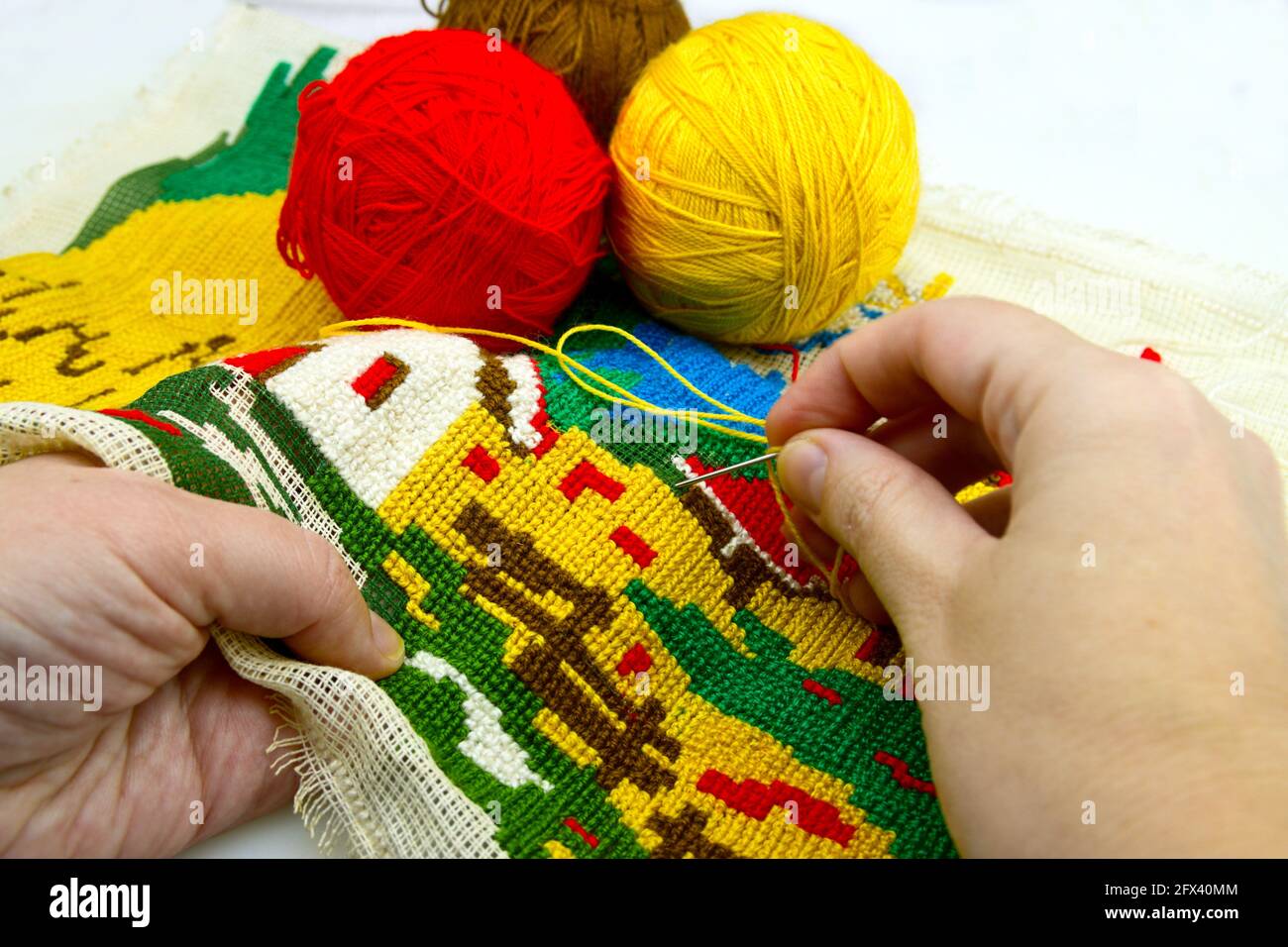 A woman's hands completing a multi-colored drawing on a cross stitch ...