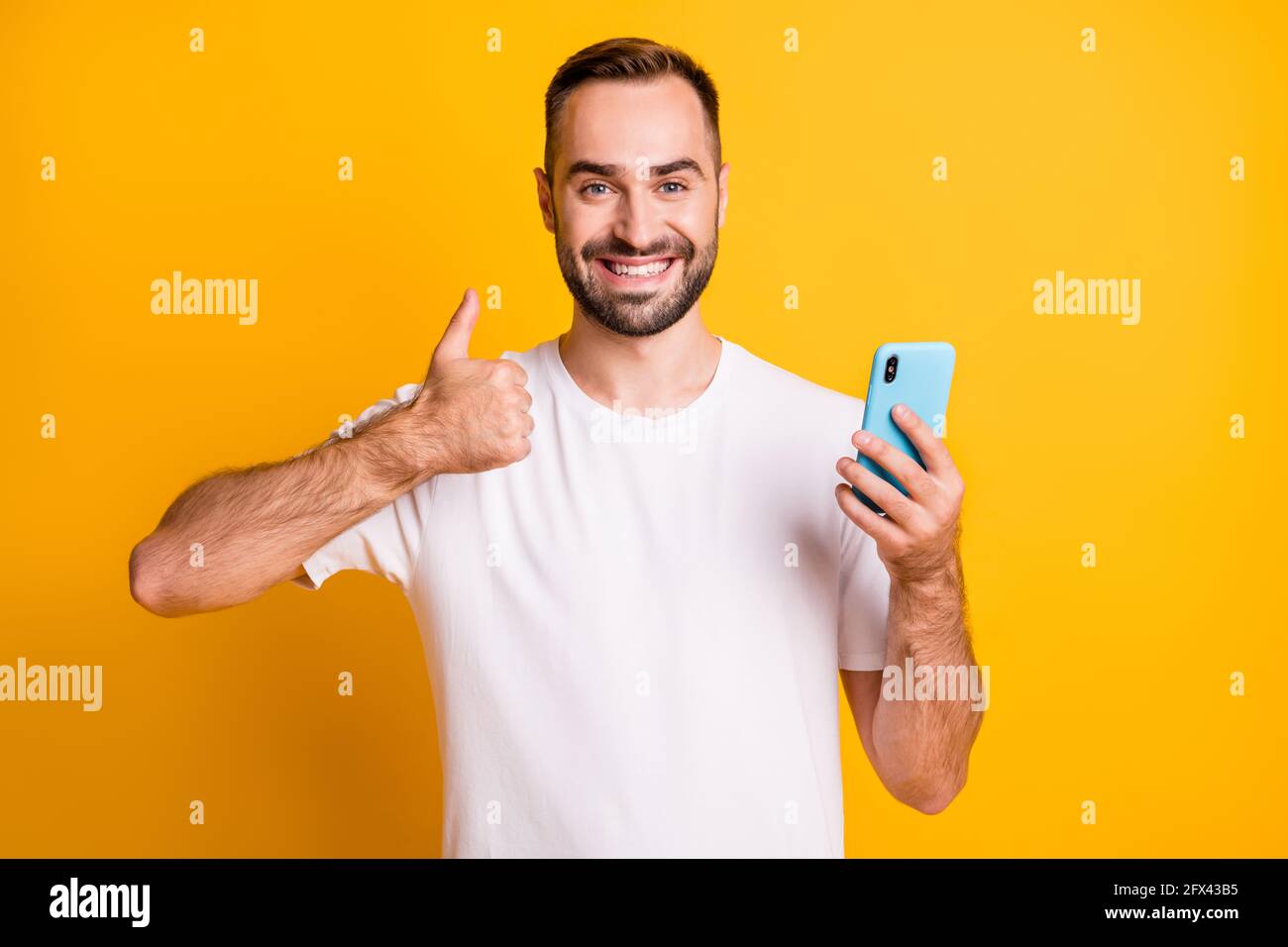 Portrait of optimistic guy hold telephone show thumb up wear white t ...