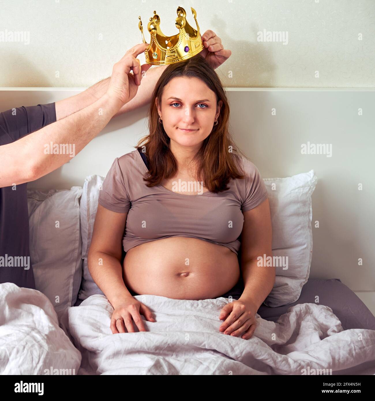 A man puts a crown on a pregnant woman. Husband and wife with a coronet on their head Stock ...