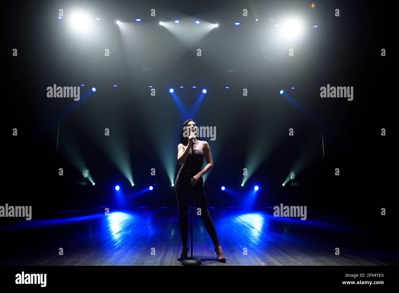 Singer perform on stage of nightclub in front of bright screen. Dark ...