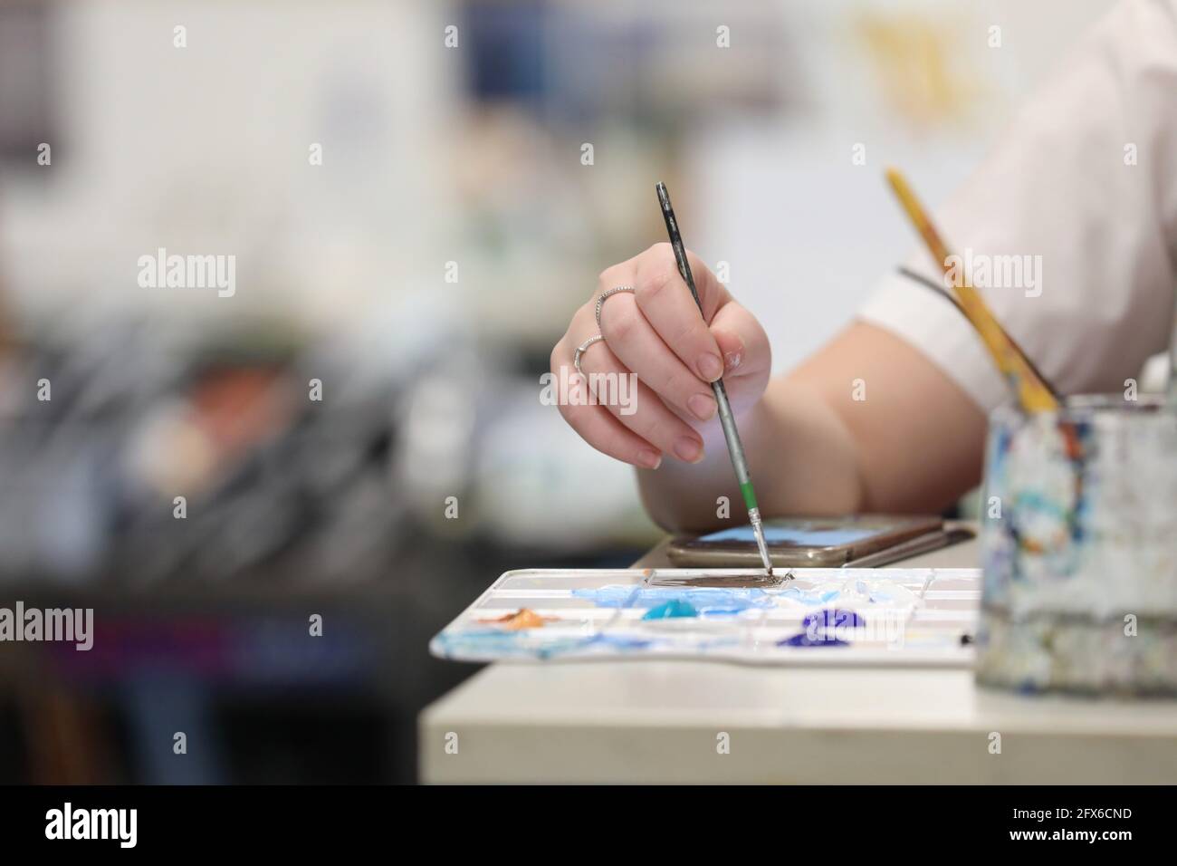 A student's hand isolated holding a paint brush mixing paints at a ...