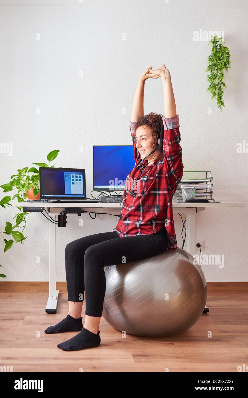 Woman stretches while working sitting on a fitball in front of her ...