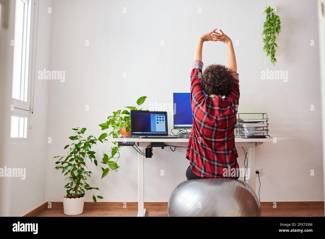 Woman stretches while working sitting on a fitball in front of her ...