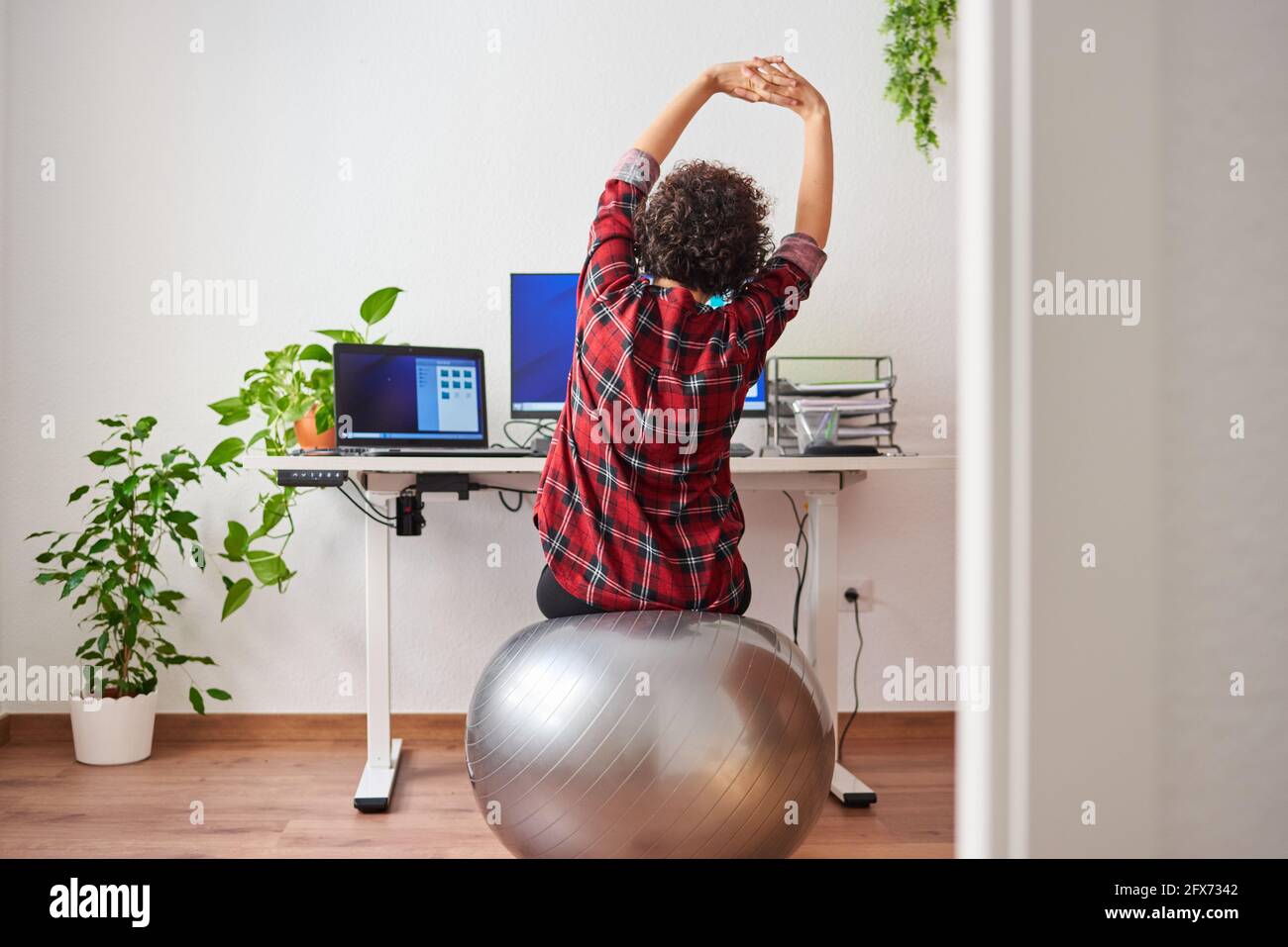 Woman stretches while working sitting on a fitball in front of her ...