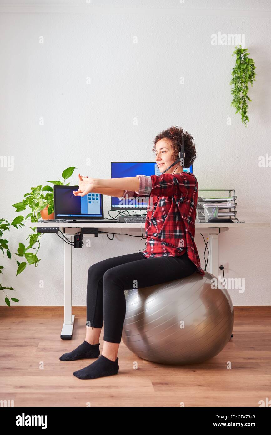 Woman stretches while working sitting on a fitball in front of her ...
