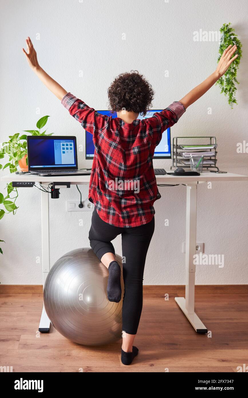 Woman stretches while working at an adjustable desk standing with one ...