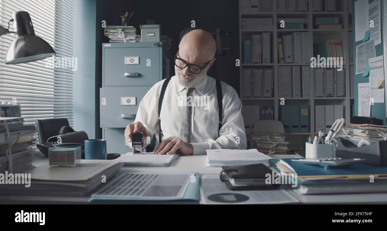 Corporate businessman sitting at office desk and stamping paperwork ...