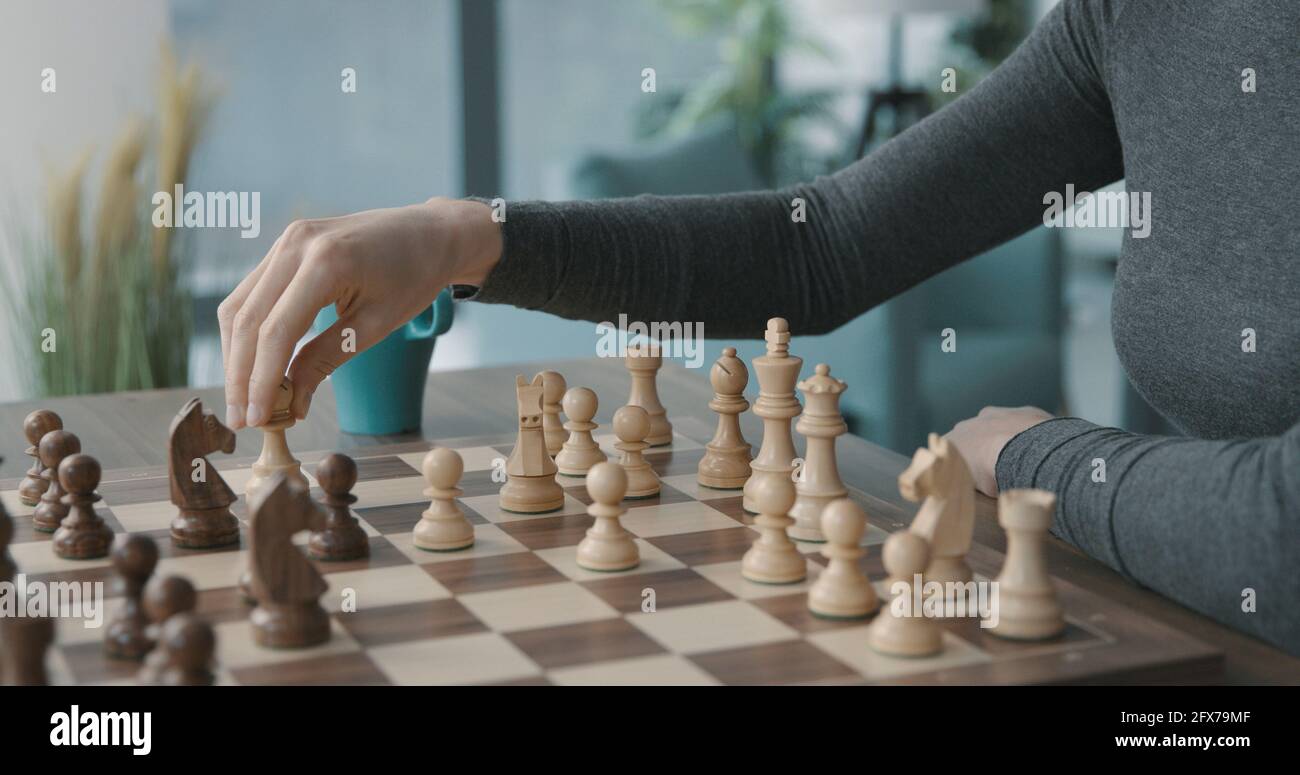 Woman playing chess at home, she is moving a pawn on the chessboard ...