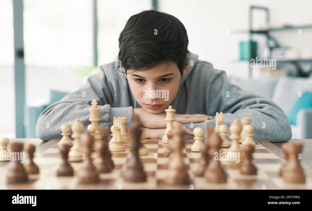 Young smart boy playing chess at home, he is focused and looking at the ...