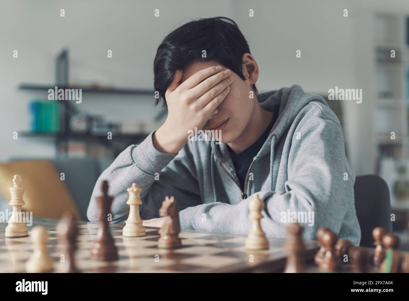 Boy playing chess and losing the game, he is disappointed and covering ...
