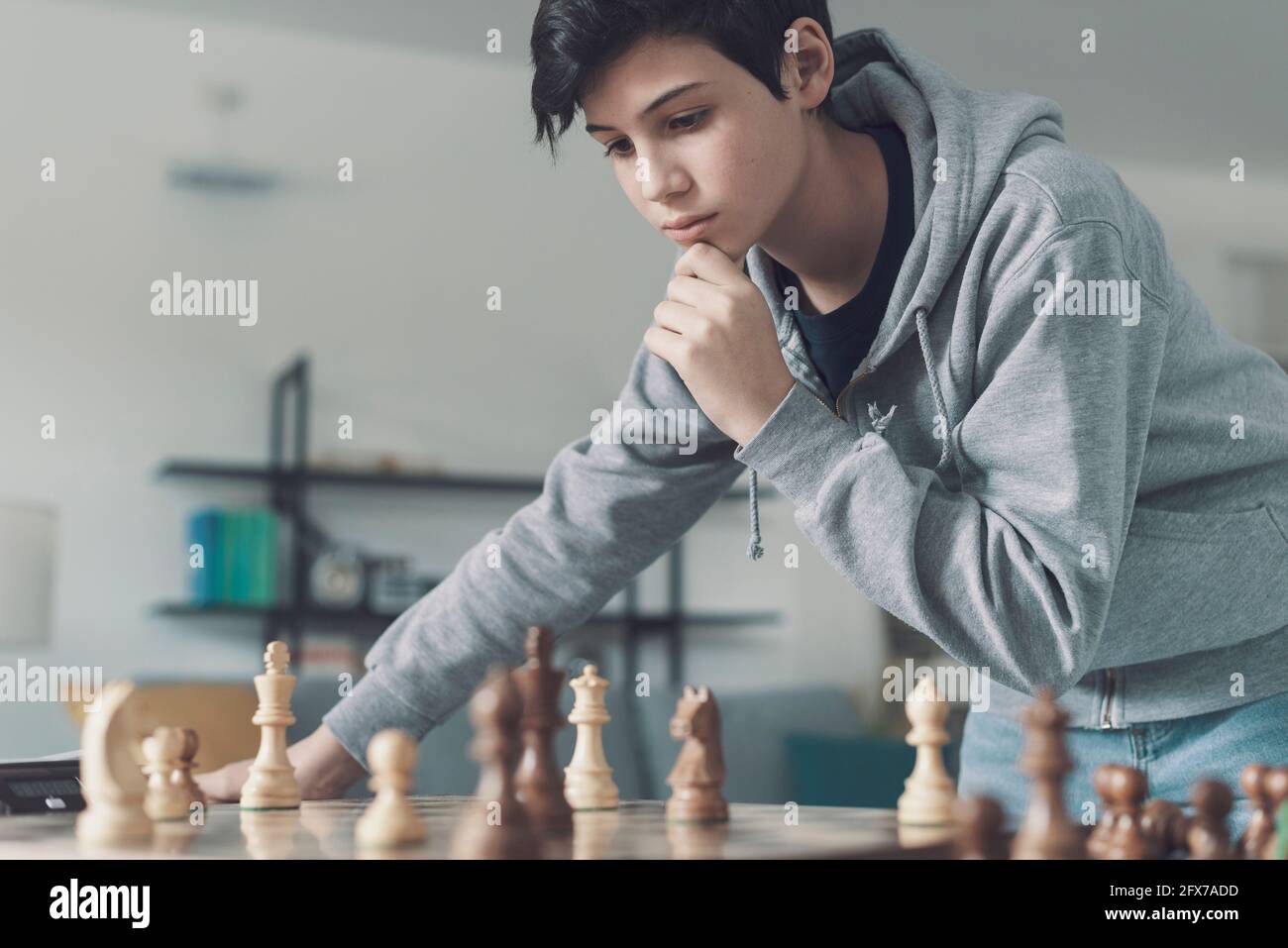 Confident smart boy playing chess at home, he is thinking and looking ...