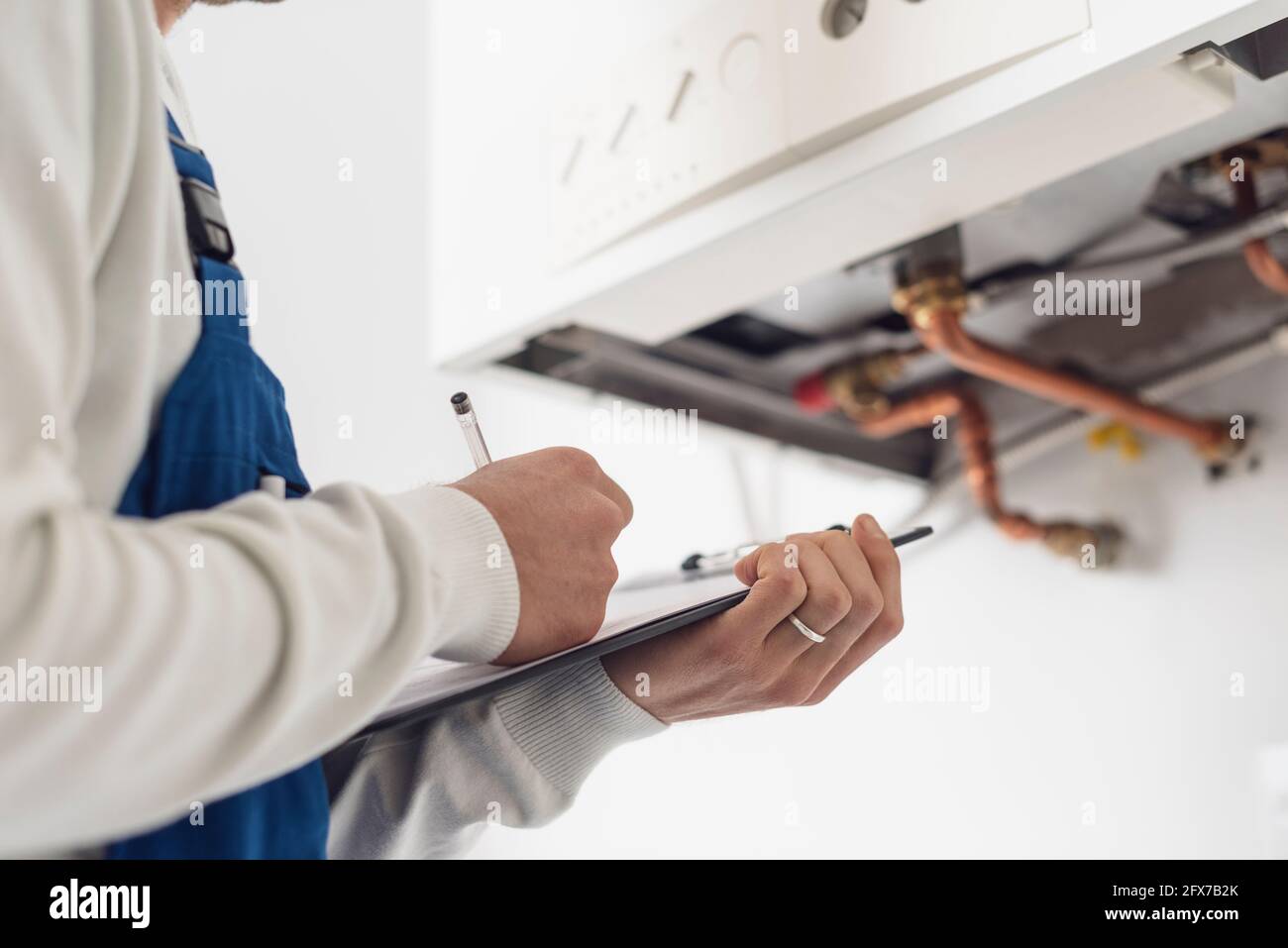 Professional plumber checking a boiler at home and writing on a ...