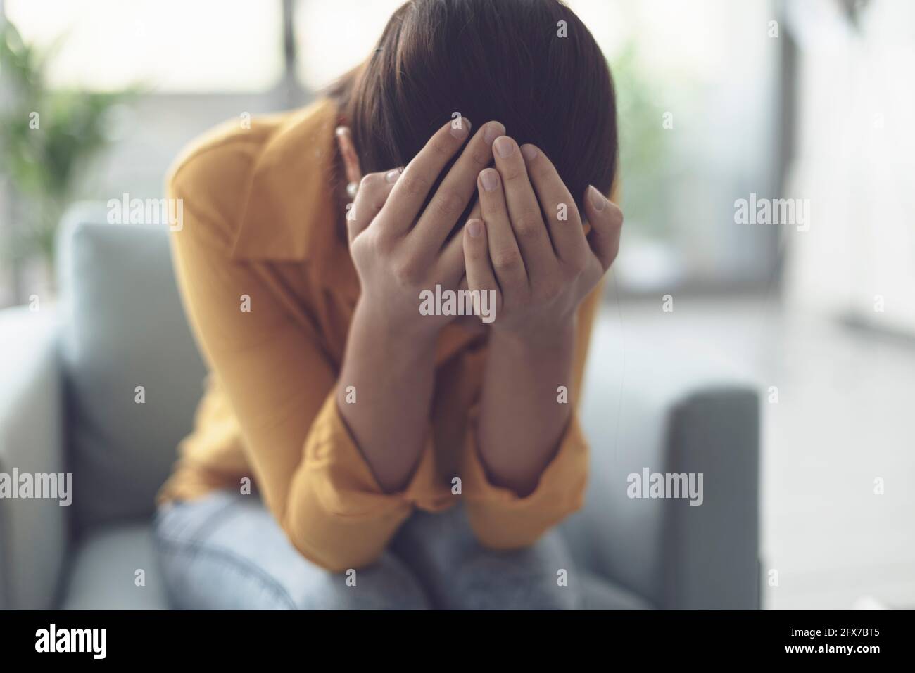 Young sad woman sitting in the living room, she is crying and covering ...