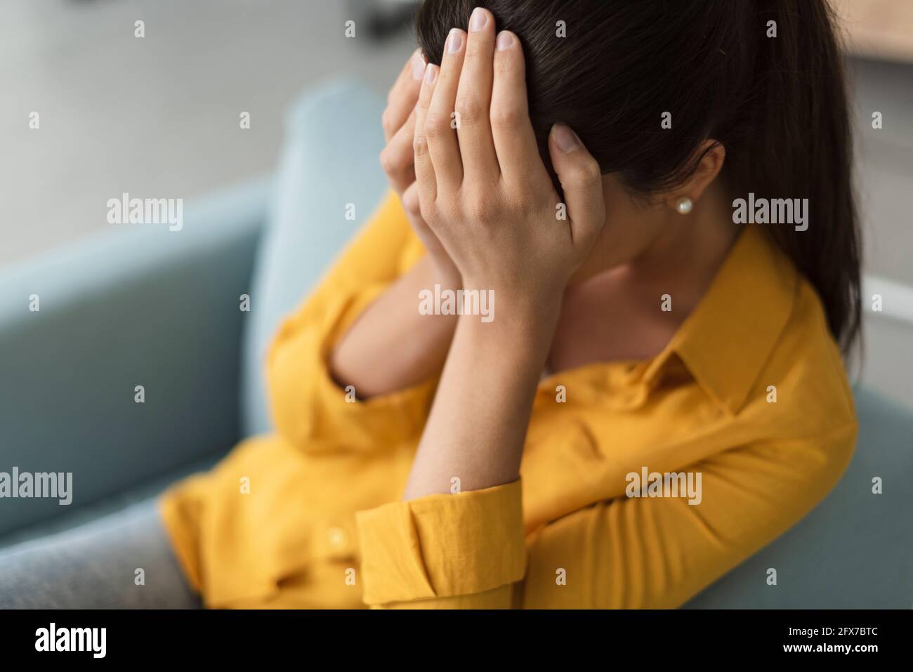 Young sad woman sitting in the living room, she is crying and covering ...
