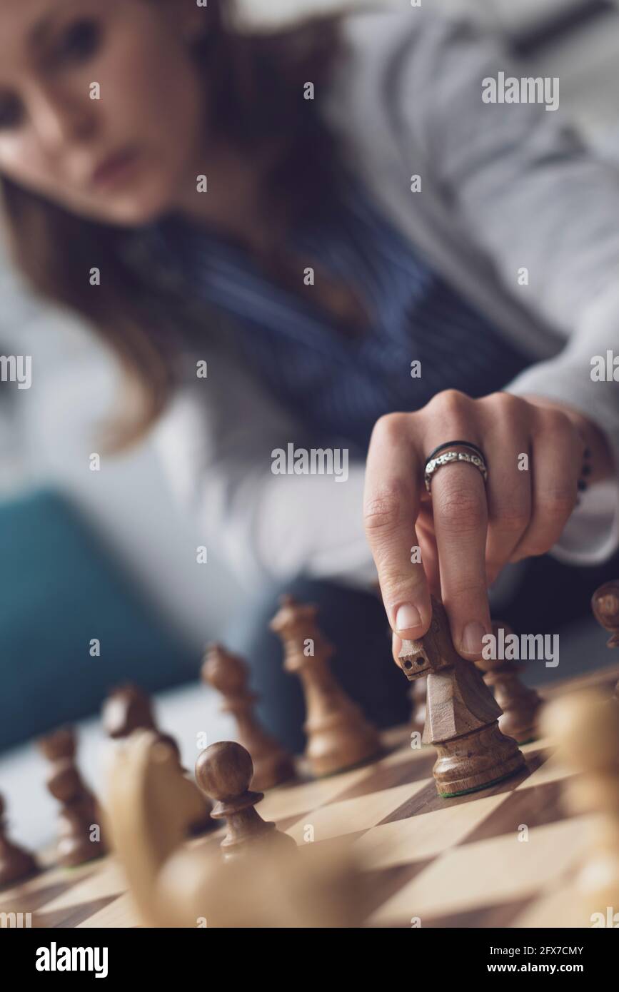 Young woman playing chess, she is moving a piece on the chessboard ...