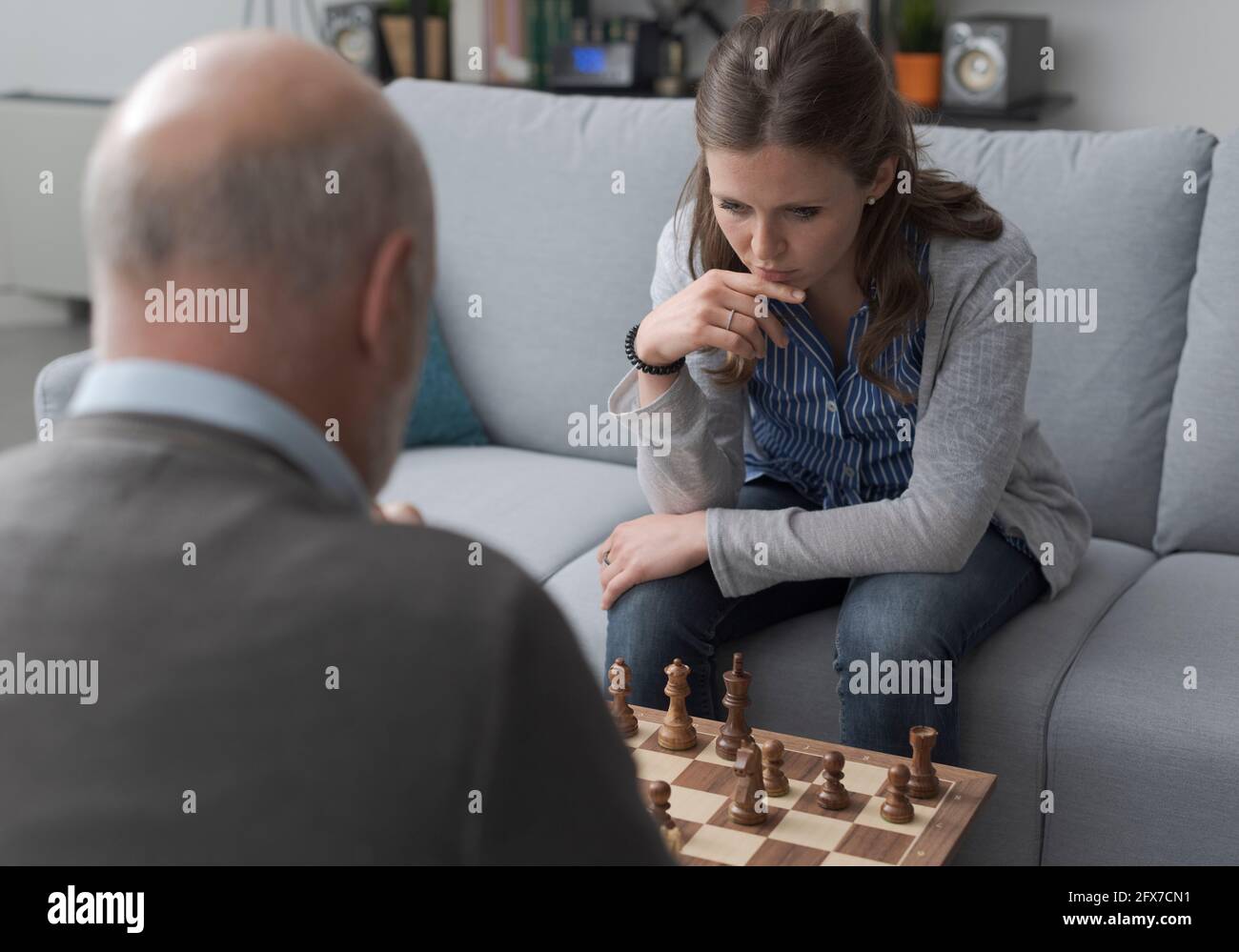 Two people playing chess at home in the living room, they are focused ...