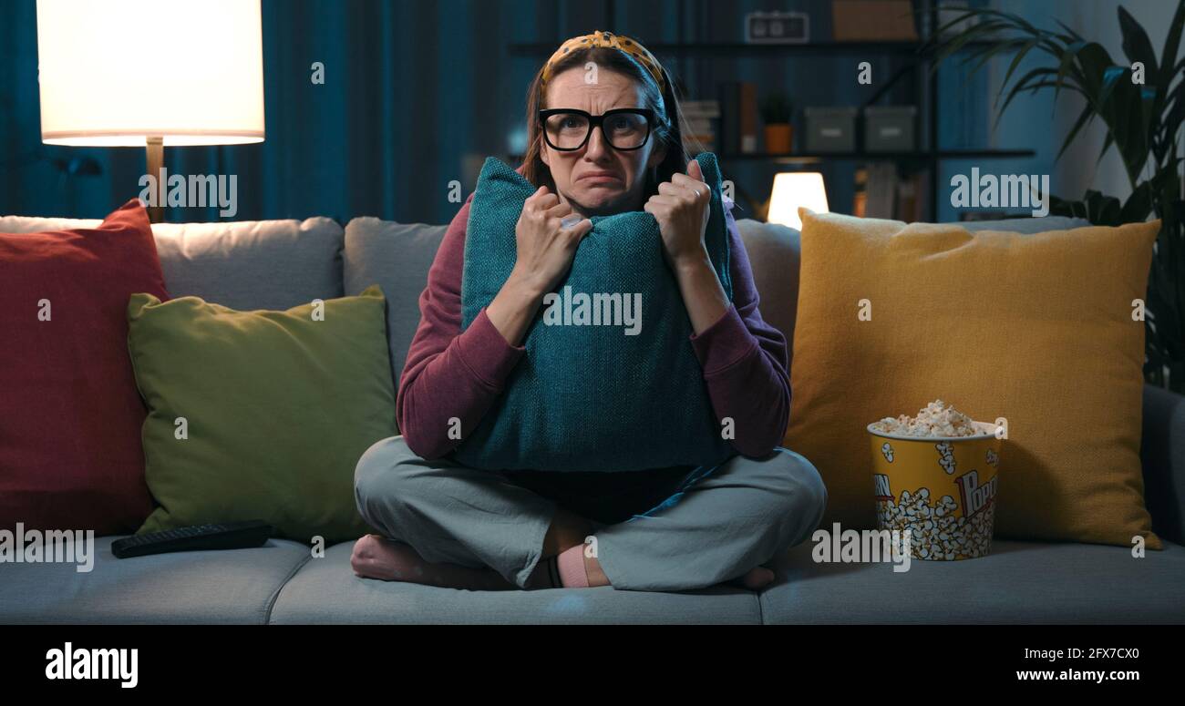 Frightened woman sitting on the couch and watching a horror movie on TV ...