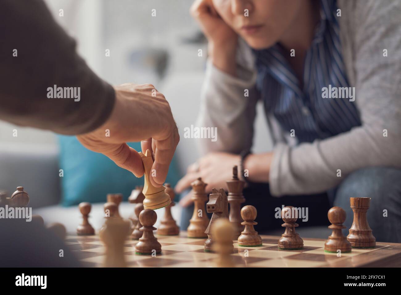 Focused people playing chess together at home, the man is moving a ...